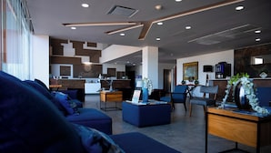 Um saguão de hotel moderno com áreas de estar, um balcão de recepção e uma cozinha ao fundo.