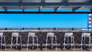 Um bar no terraço com parede de padrão geométrico e cadeiras com estrutura de metal.