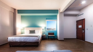 Quarto de hotel moderno com uma cama grande, área de estar e vista para a cidade pela janela.