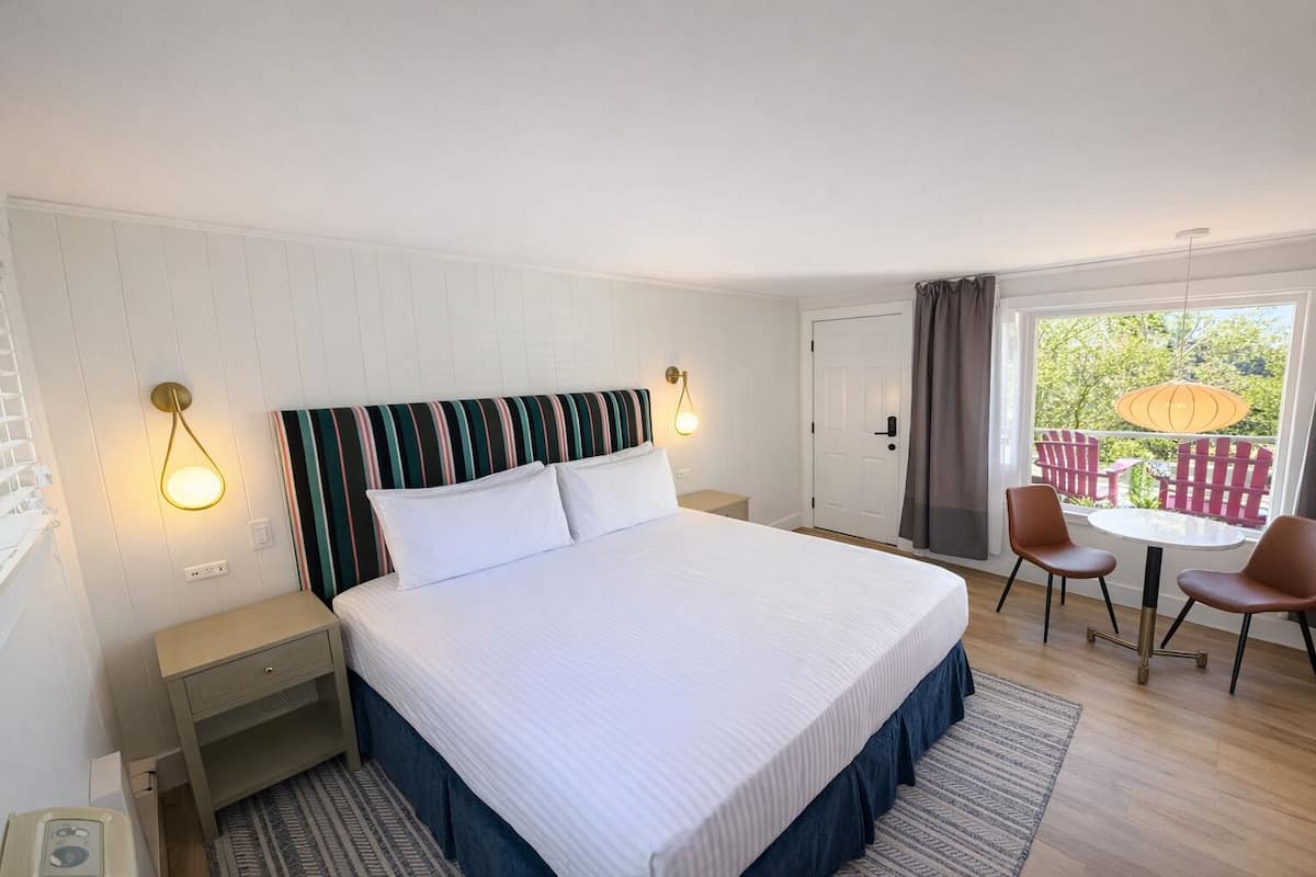 Quarto de hotel com uma cama grande, mesas de cabeceira, uma pequena mesa com cadeiras e vista para o exterior.