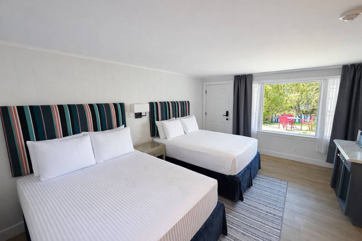 Quarto de hotel com duas camas, uma escrivaninha, janela com vista para o exterior e uma porta.
