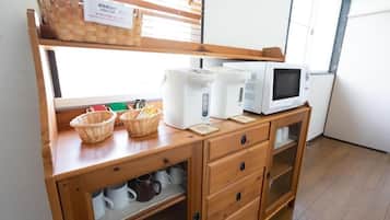 Uma cozinha compacta com micro-ondas, torradeira e cafeteira em uma bancada de madeira. Há cestos e uma placa indicando o uso de uma xícara usada.