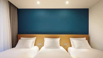 Quarto de hotel com três camas, cabeceira de madeira e uma parede em azul.