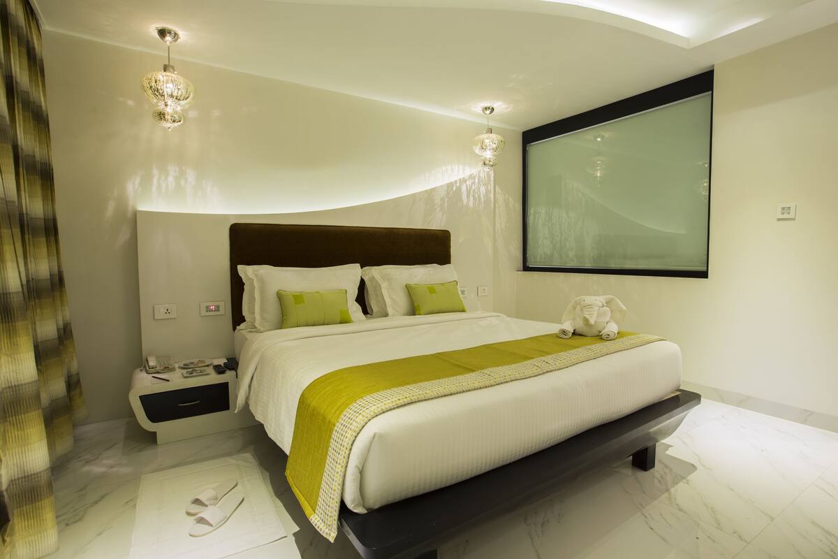 Quarto de hotel moderno com uma cama grande, mesas de cabeceira e uma janela ampla.