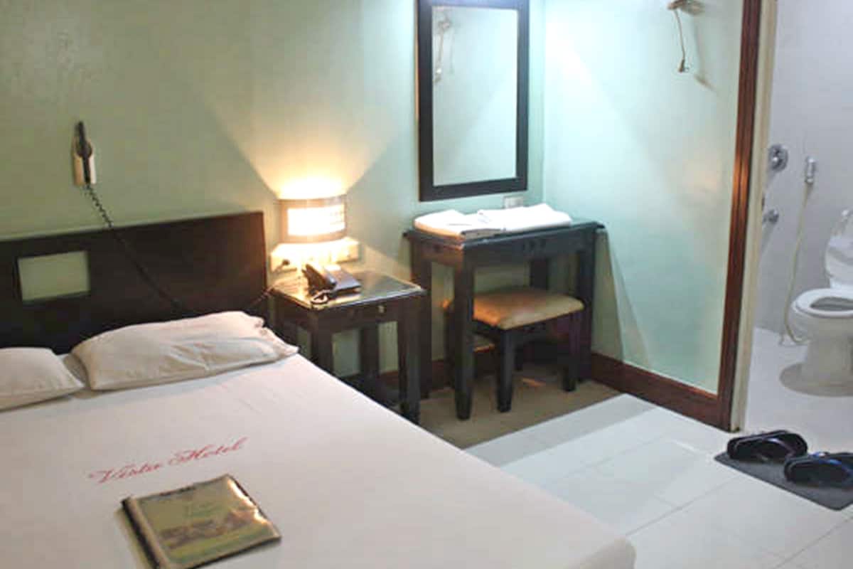 Quarto de hotel com cama, escrivaninha, espelho, telefone e zona de duche.