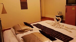 Quarto de hotel com cama, almofadas, toalha, teclado, pequena mesa com um vaso, televisão e frigorífico.