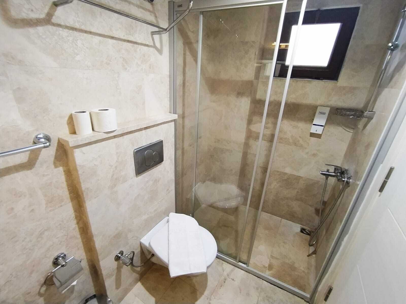 Uma casa de banho moderna com chuveiro em cabine de vidro, sanita e suporte para toalhas.