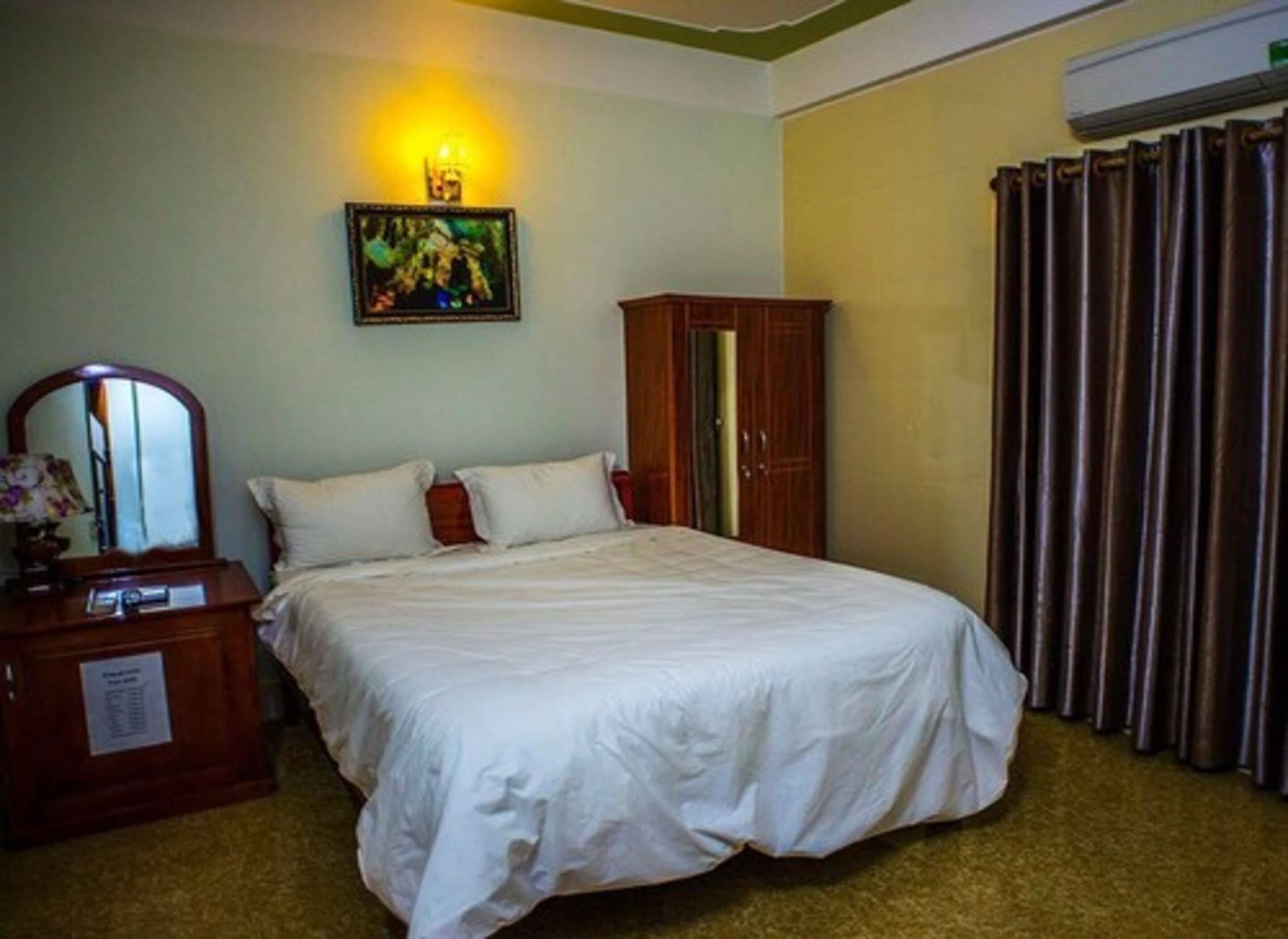 Quarto de hotel com uma cama grande, um guarda-roupa de madeira, um espelho e um quadro na parede.