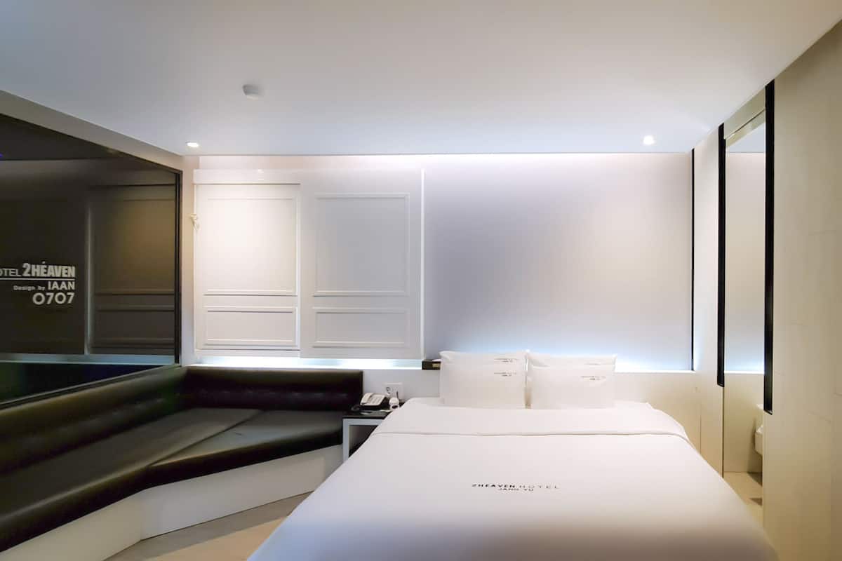 Quarto de hotel moderno com uma cama grande, área de estar e um espelho amplo.