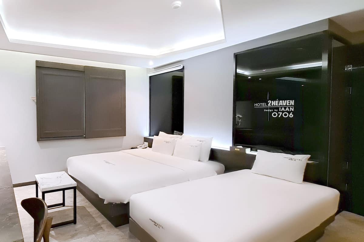 Quarto de hotel moderno com duas camas, uma escrivaninha, uma cadeira e um espelho grande.