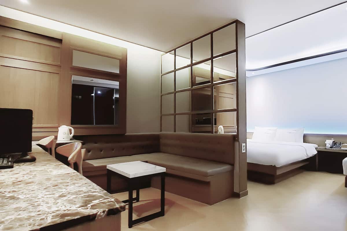Quarto de hotel moderno com sofá, cama, escrivaninha com computador e uma janela grande.