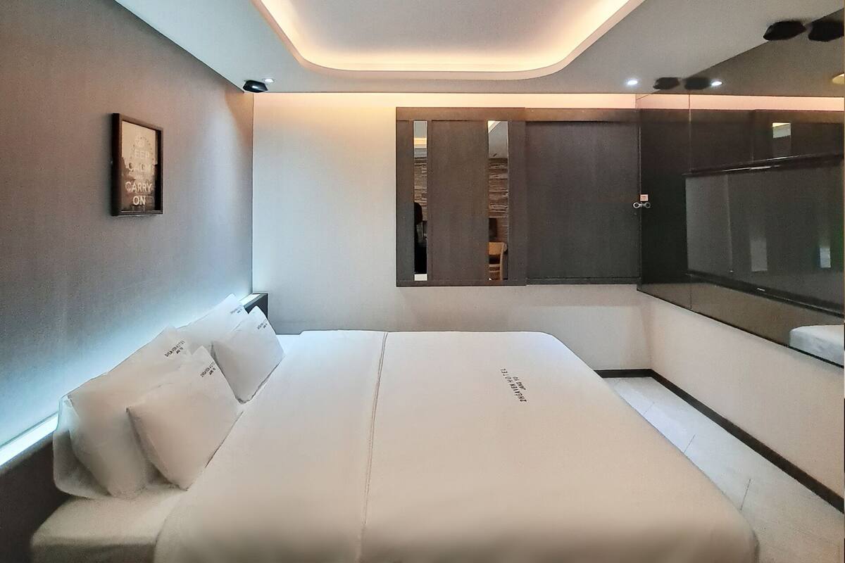 Quarto moderno com cama, mesa de cabeceira, espelho e armário embutido.
