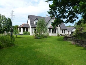 Uma casa de dois andares com gramado bem cuidado e uma grande árvore no quintal da frente.