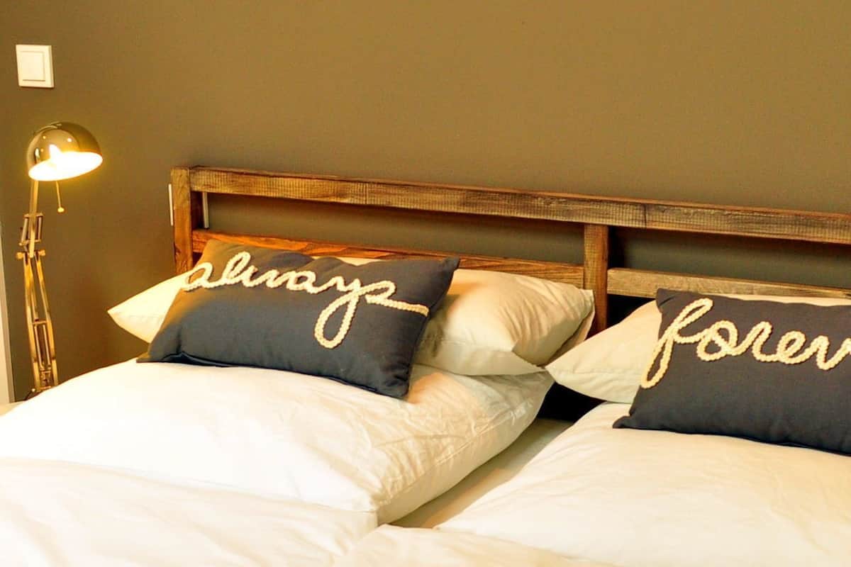Uma cama de casal com roupa de cama branca e duas almofadas bordadas.