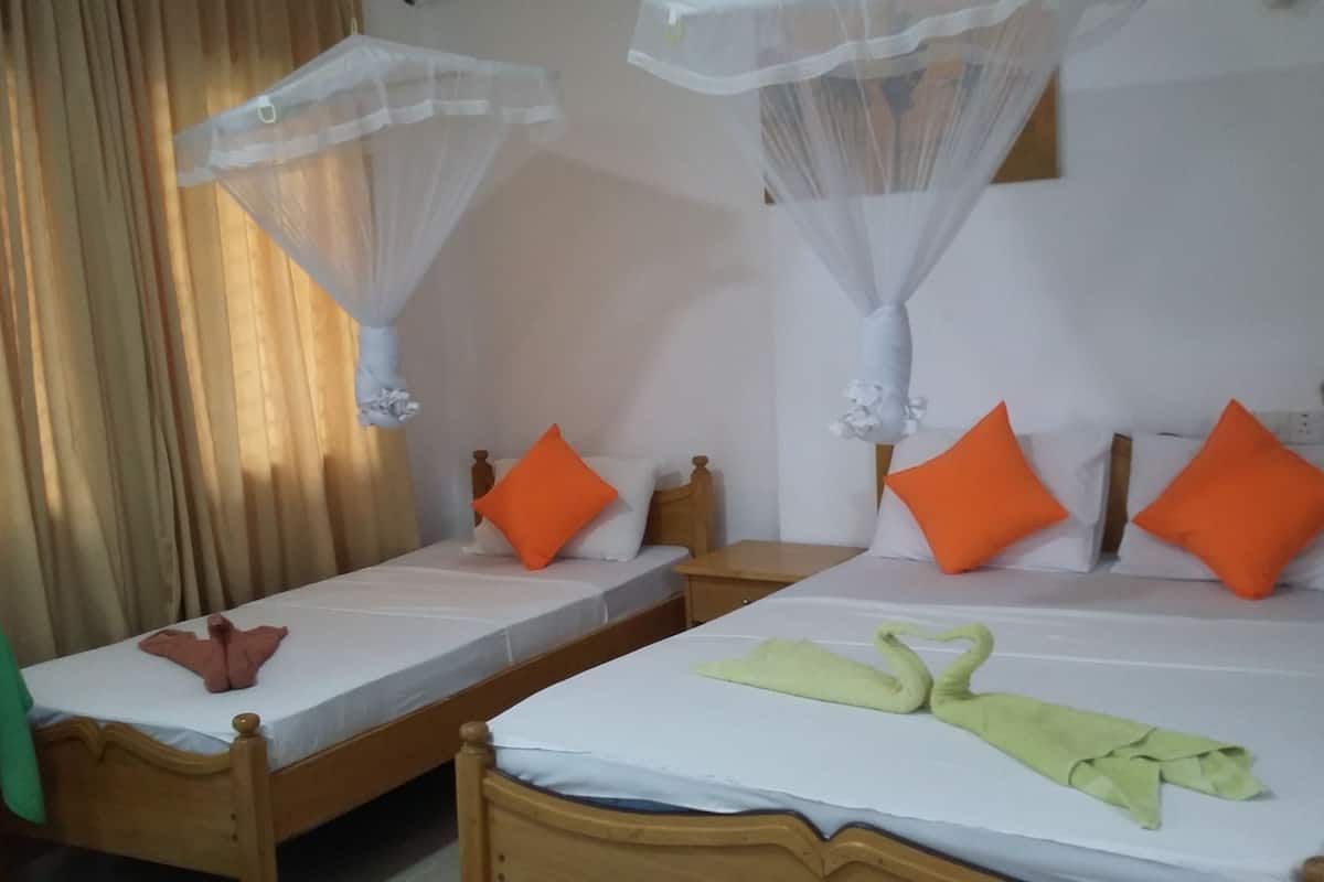 Duas camas de solteiro com estrutura de madeira e roupa de cama branca, cada uma com uma almofada laranja e um mosquiteiro sobre ela.