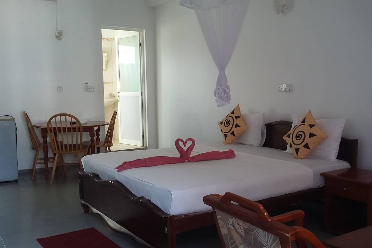 Quarto de hotel com cama, escrivaninha, cadeira e banheiro visível através de uma porta aberta.