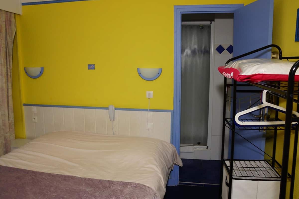 Quarto com beliche, cama de solteiro, banheiro com chuveiro e porta que dá para outro quarto.