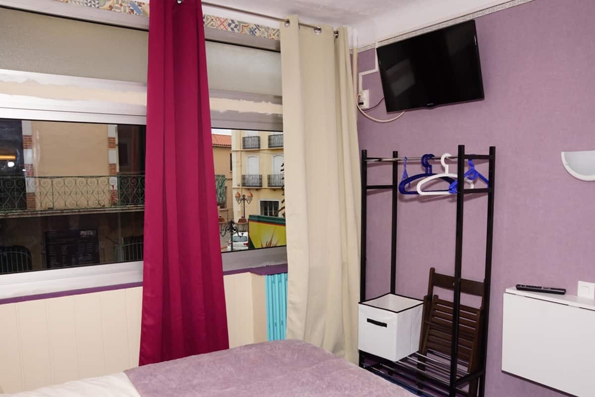 Quarto com cama, televisão, escrivaninha e cadeira.