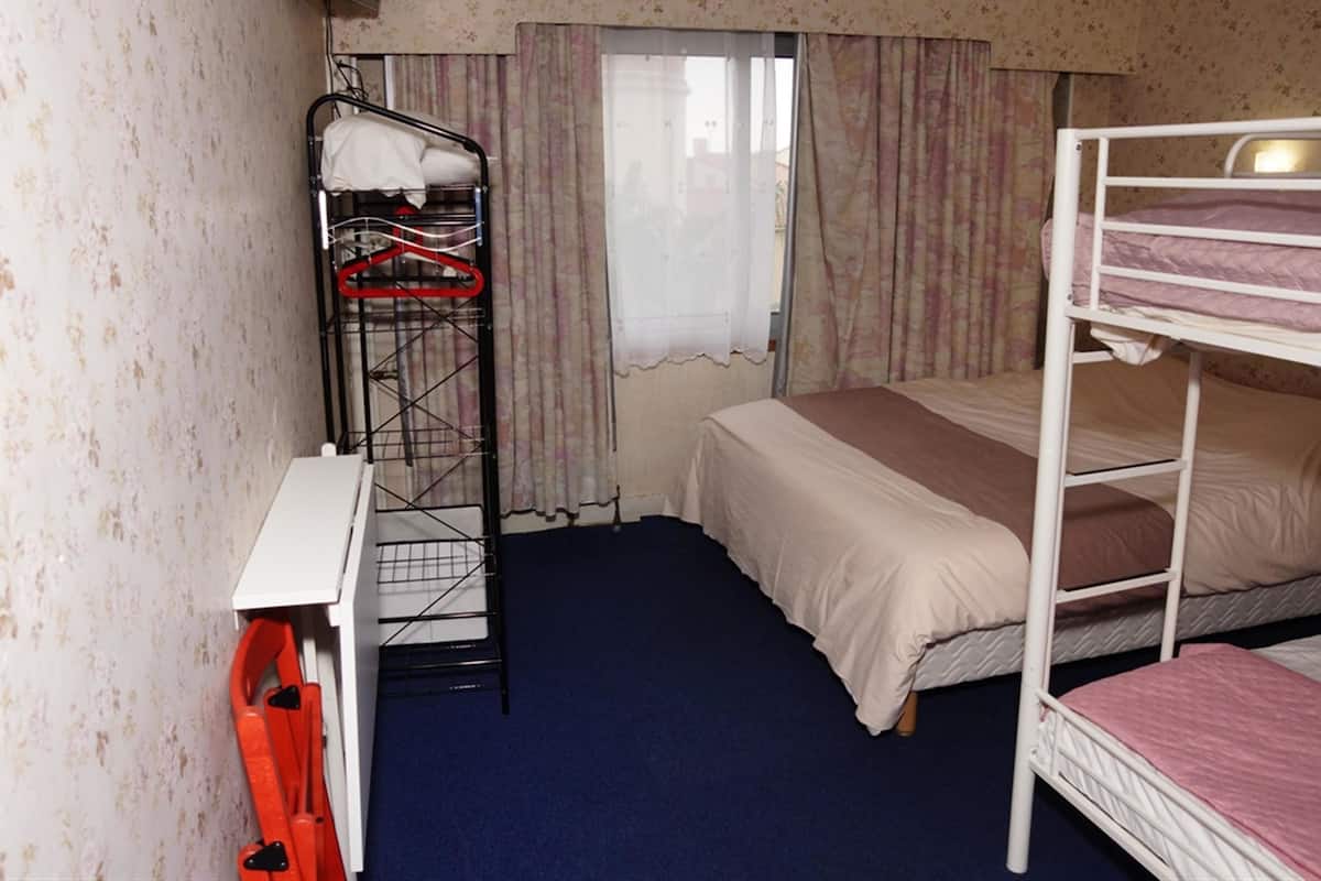 Quarto com beliche, escrivaninha com cadeira, cabideiro e janela com cortinas.