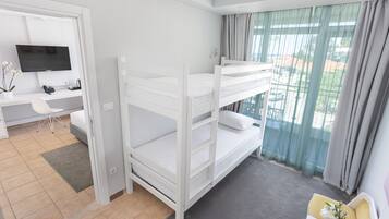 Quarto de hotel moderno com beliche, escrivaninha com cadeira, televisão e uma janela grande com cortinas.