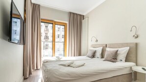 Quarto de hotel com uma cama grande, televisão na parede e janela com cortinas.