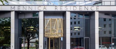 A entrada do edifício Mennica Residence com uma grande placa '4A' e portas de vidro.