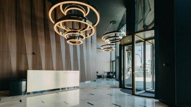 Um hall moderno com balcão de recepção, amplas janelas e uma série de luminárias circulares.