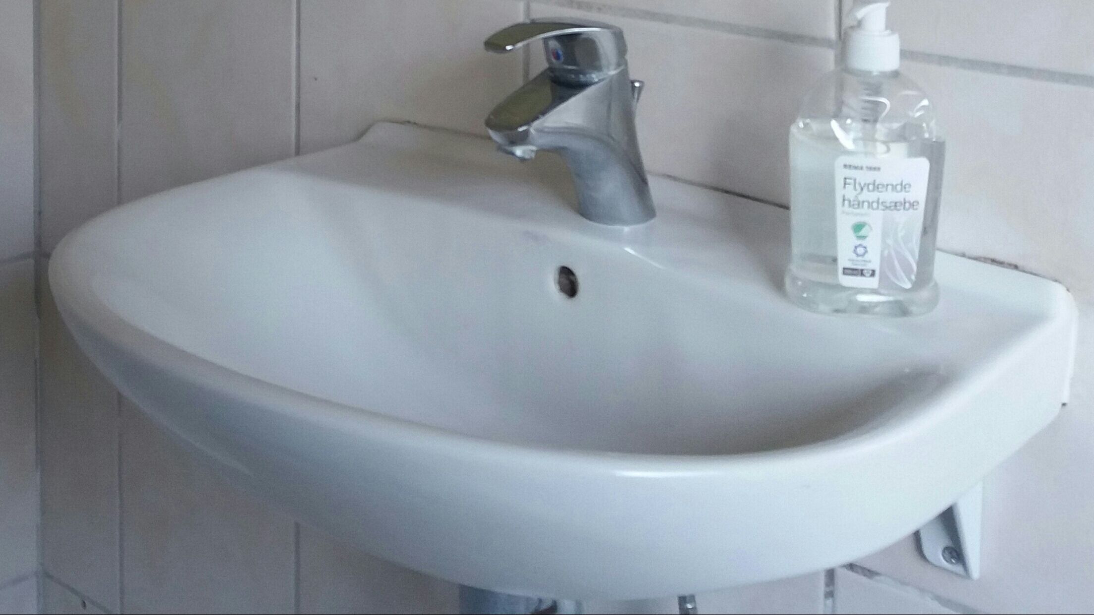 Uma pia de banheiro branca com uma torneira moderna e um frasco de álcool em gel.