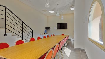 Uma sala de conferências com uma longa mesa de madeira, cadeiras vermelhas, uma televisão e uma escada.