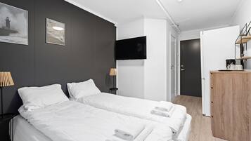 Quarto de hotel moderno com duas camas, televisão de tela plana, um armário de madeira e obras de arte nas paredes.