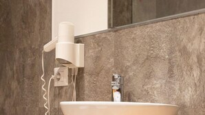 Casa de banho com lavatório branco, porta-toalhas e secador de cabelo.