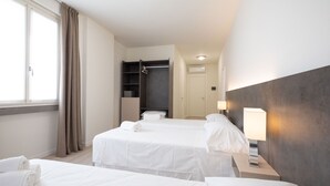 Quarto de hotel com duas camas, um guarda-roupa, um espelho e um abajur.