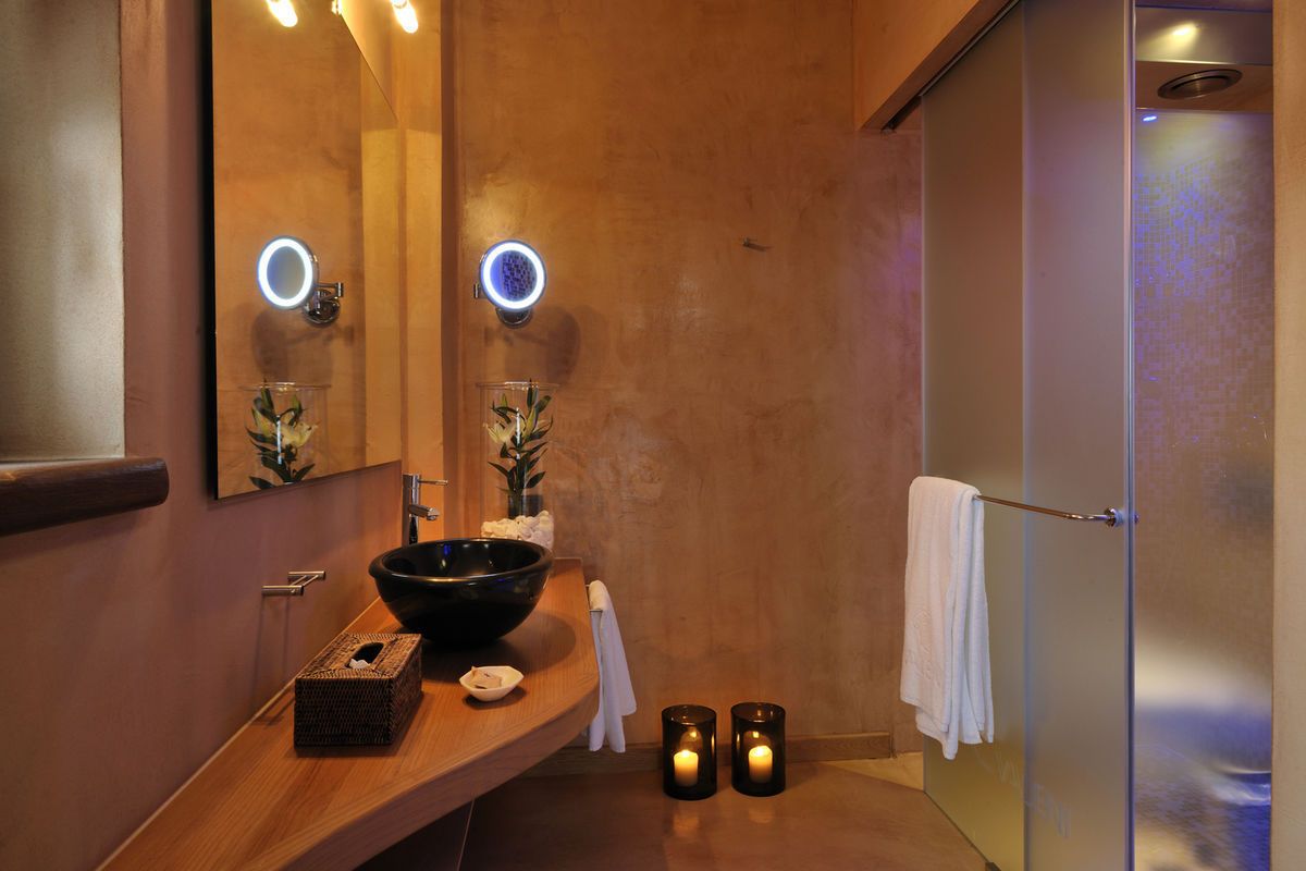 Uma casa de banho moderna com toucador de madeira, um espelho grande com luzes, lavatório em cerâmica preta e duas velas.