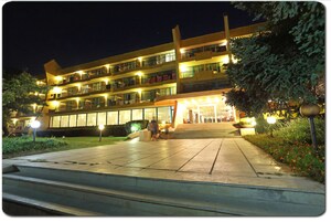 Um hotel de vários andares com uma entrada bem iluminada e um jardim ajardinado.
