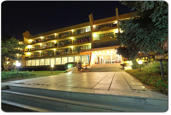 Um hotel de vários andares com uma entrada bem iluminada e um jardim ajardinado.