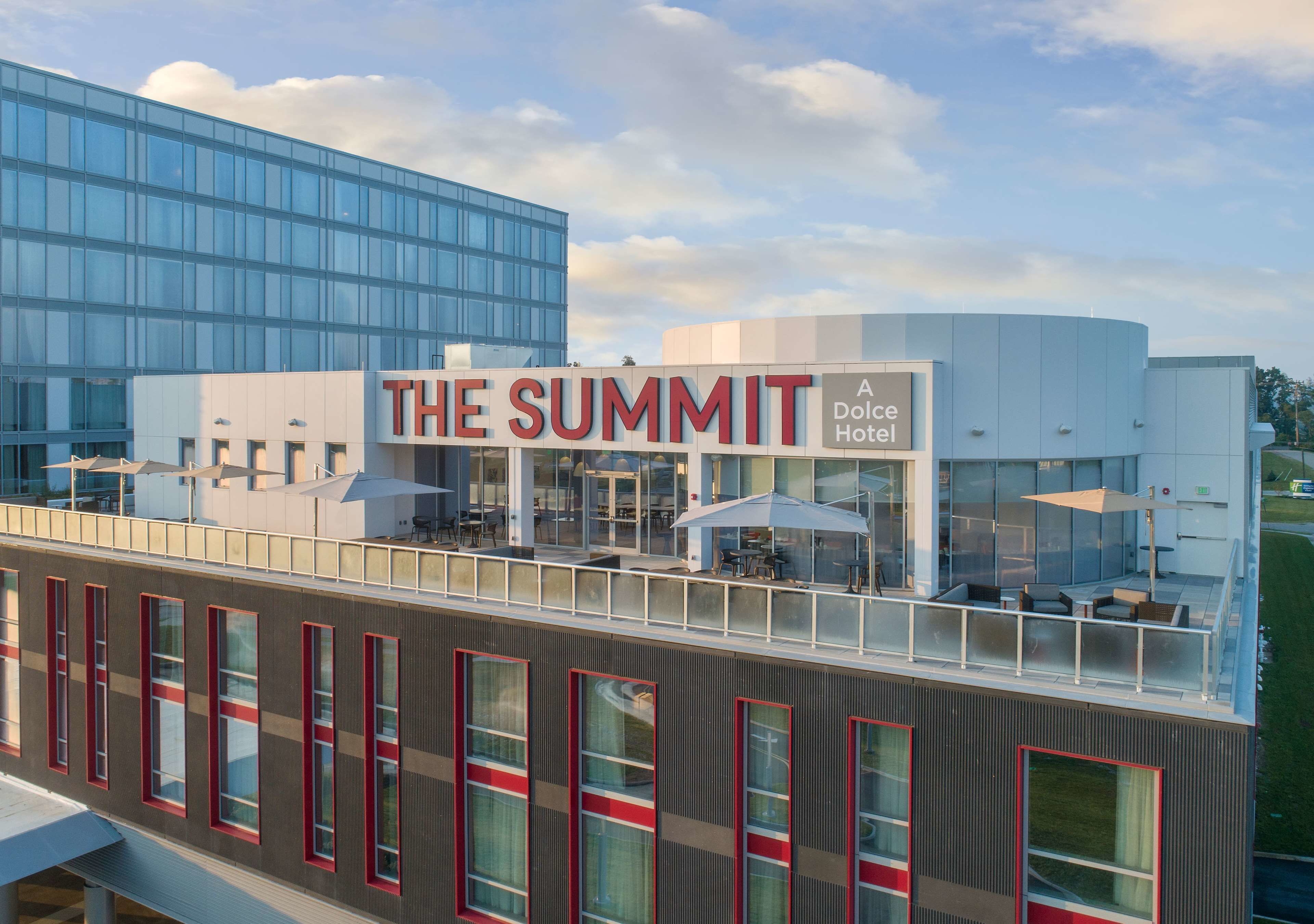 Um hotel chamado "The Summit", com design arquitetônico moderno, apresentando uma placa em destaque e área externa com mesas.