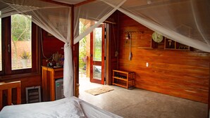 Um quarto com uma cama, uma escrivaninha pequena, uma prateleira de madeira e uma porta que dá para o exterior.