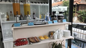 Um buffet de café da manhã com diversas opções de alimentos e bebidas, incluindo suco de maracujá, suco de abacaxi e café.