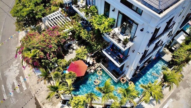 Um hotel moderno com piscina no terraço, rodeado por vegetação exuberante e palmeiras.
