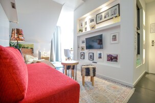 Uma sala de estar moderna com um sofá vermelho, uma mesa redonda pequena e uma TV fixada na parede.