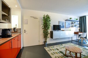Uma cozinha moderna com forno embutido, uma área de jantar com mesa e cadeiras, uma planta em vaso e uma televisão na parede.