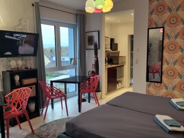 Quarto de hotel moderno com uma cama grande, uma escrivaninha com cadeira, televisão e vista para o exterior.