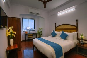 Quarto de hotel com uma cama grande, uma escrivaninha, uma cadeira e uma janela.