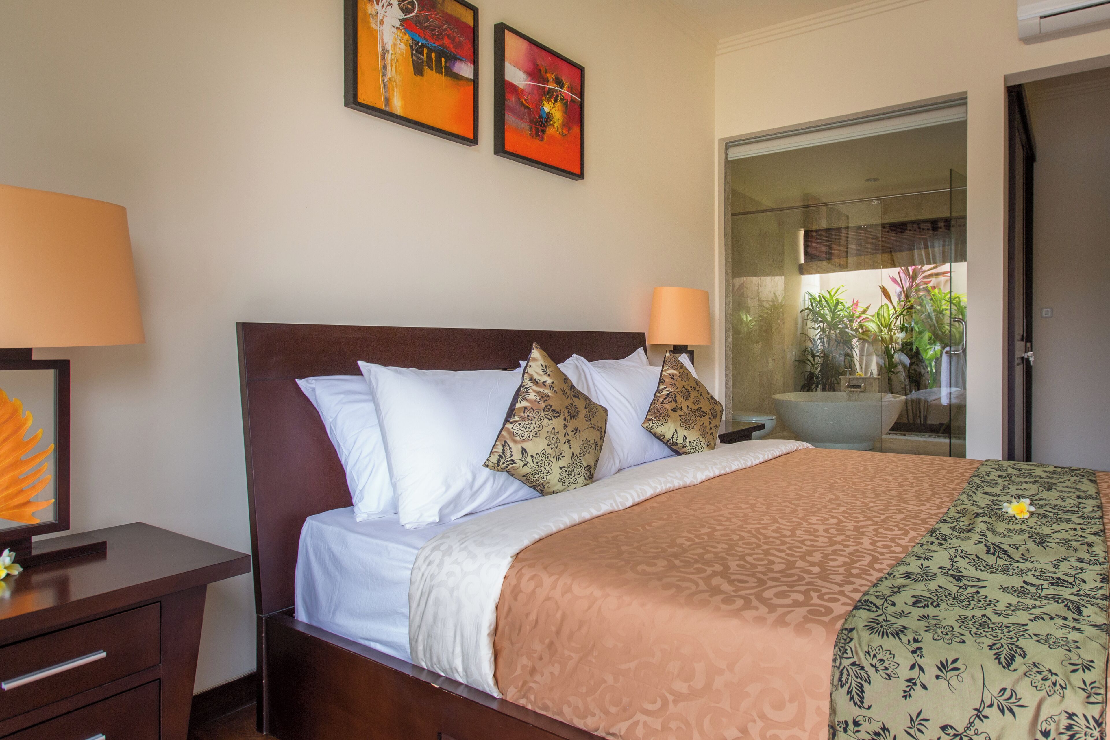 Quarto de hotel com uma cama grande, duas luminárias de cabeceira, mesa de cabeceira e janela com vista para uma piscina e plantas.