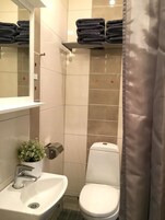 Uma casa de banho com uma pia branca, sanita e uma prateleira com toalhas dobradas.