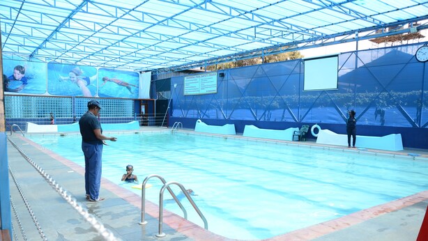 Piscina interna com trampolim, cartaz de regras de segurança e relógio na parede.