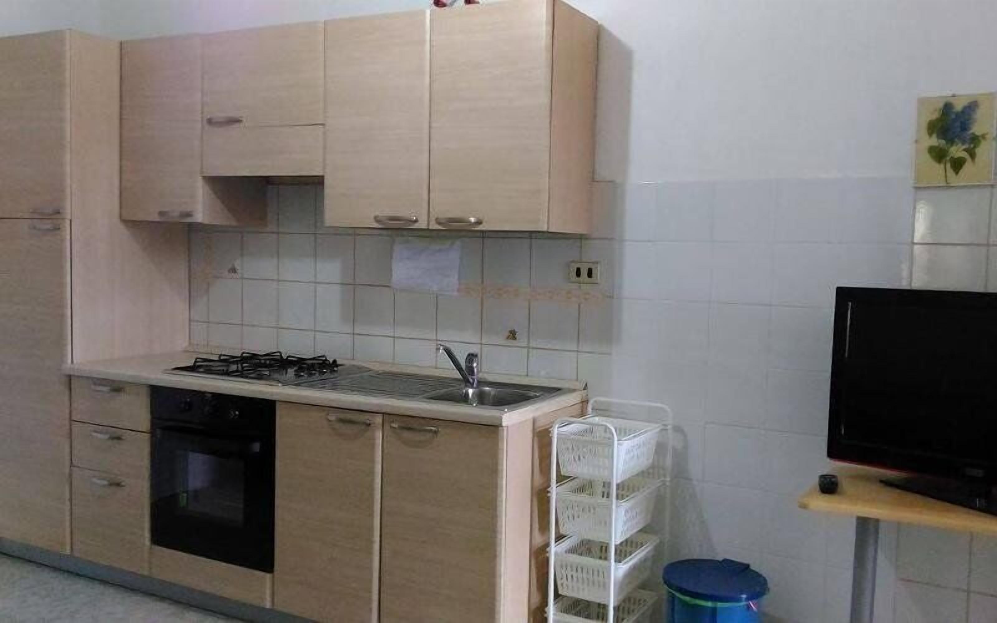 Uma cozinha compacta com armários de madeira clara, fogão a gás, pia e geladeira pequena.