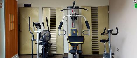Uma academia com equipamentos de exercício, um tapete de yoga e um banquinho amarelo.