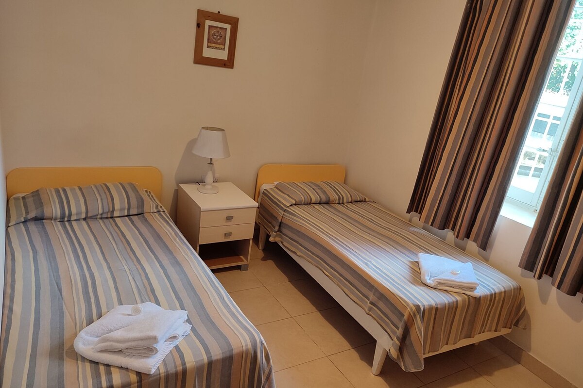 Quarto de hotel com duas camas, uma mesa de cabeceira, um abajur e um quadro pendurado na parede.