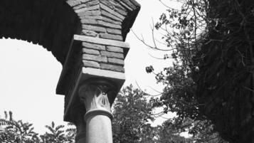 Um arco de pedra com padrão em tijolos, rodeado por folhagem.